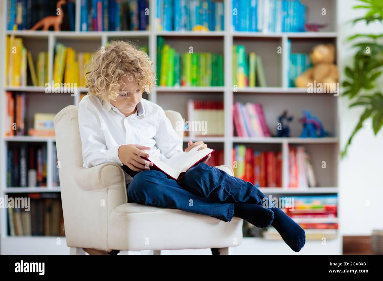 Child reading book. Kids read. Little boy at a colorful bookshelf doing ...