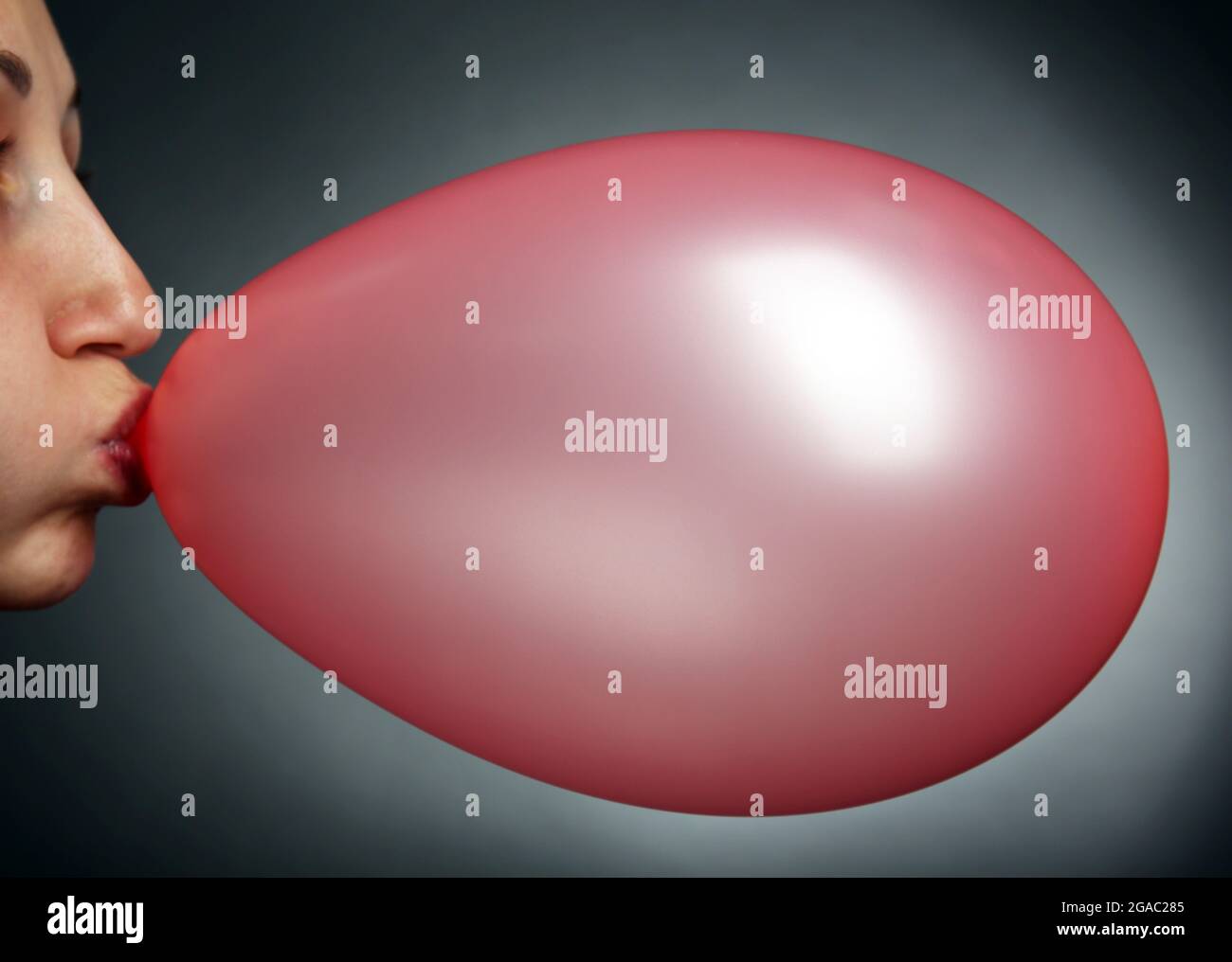 Young woman inflating balloon on gray background Stock Photo - Alamy