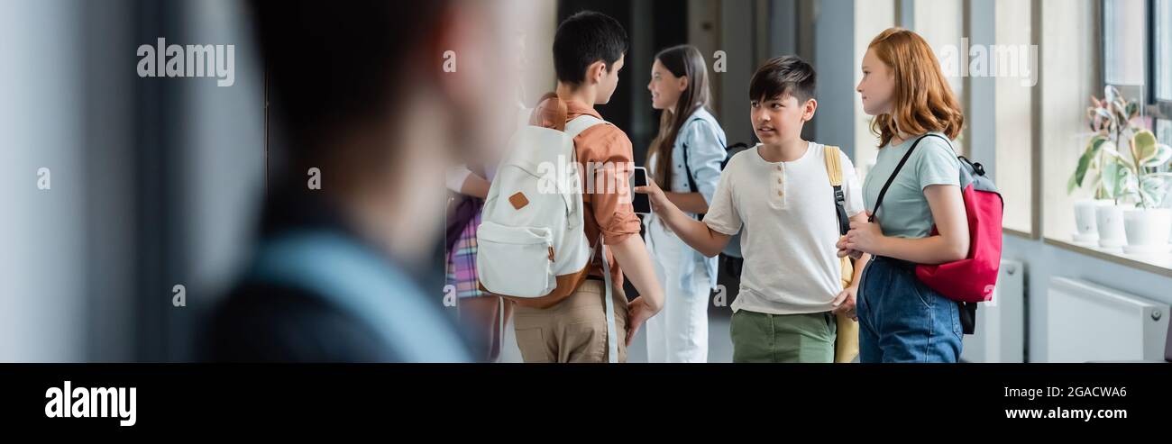 blurred boy standing alone near teenagers talking in school corridor ...