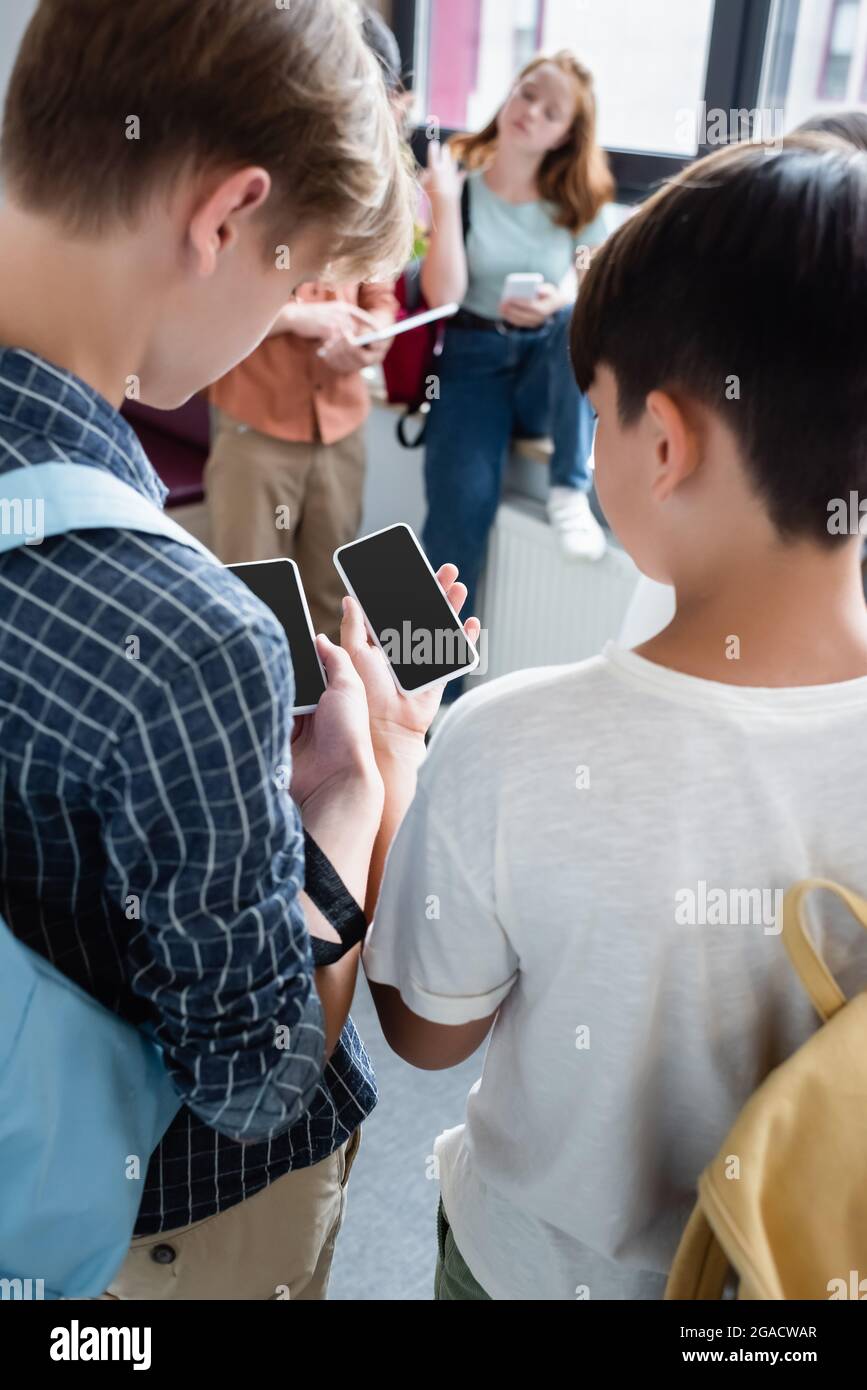 back view of schoolboys holding mobile phones with blank screen near ...