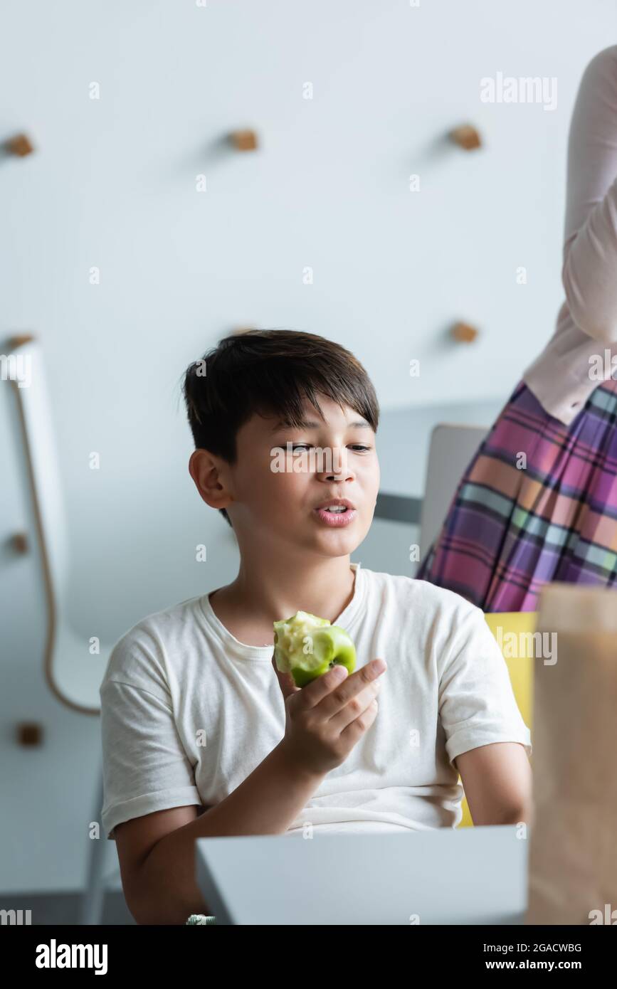 asian boy eating apple and pointing with middle finger while talking in ...