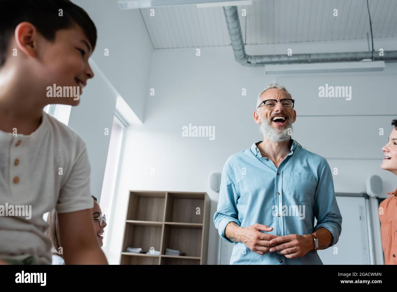 low angle view of bearded teacher laughing near multiethnic pupils in ...