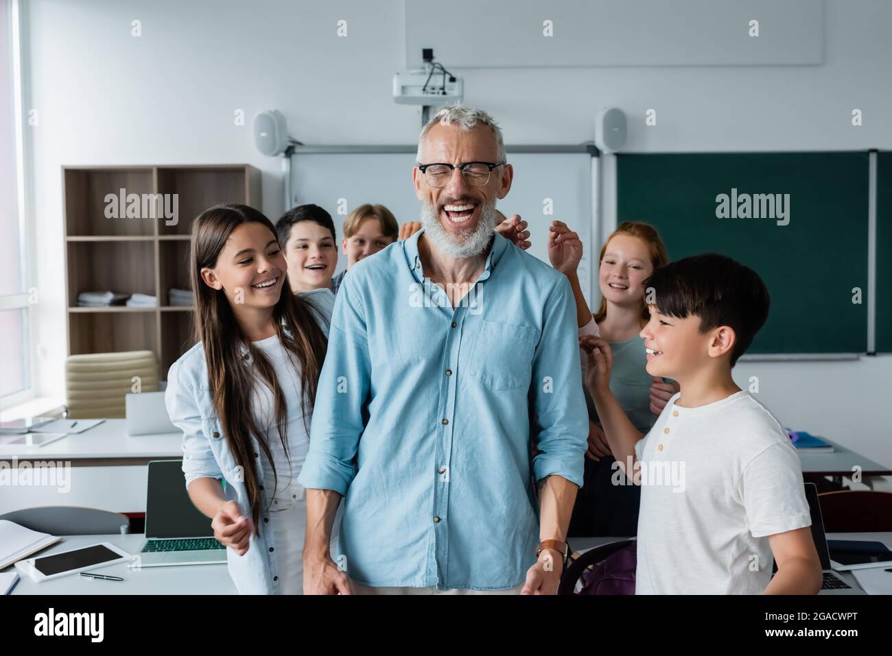 cheerful multiethnic classmates near happy teacher laughing with closed ...
