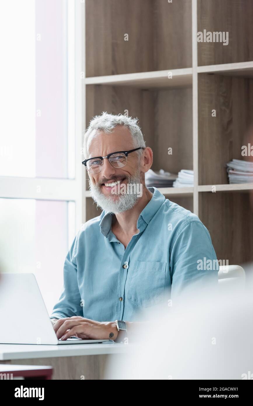 Happy teacher using laptop and looking at camera in classroom Stock ...