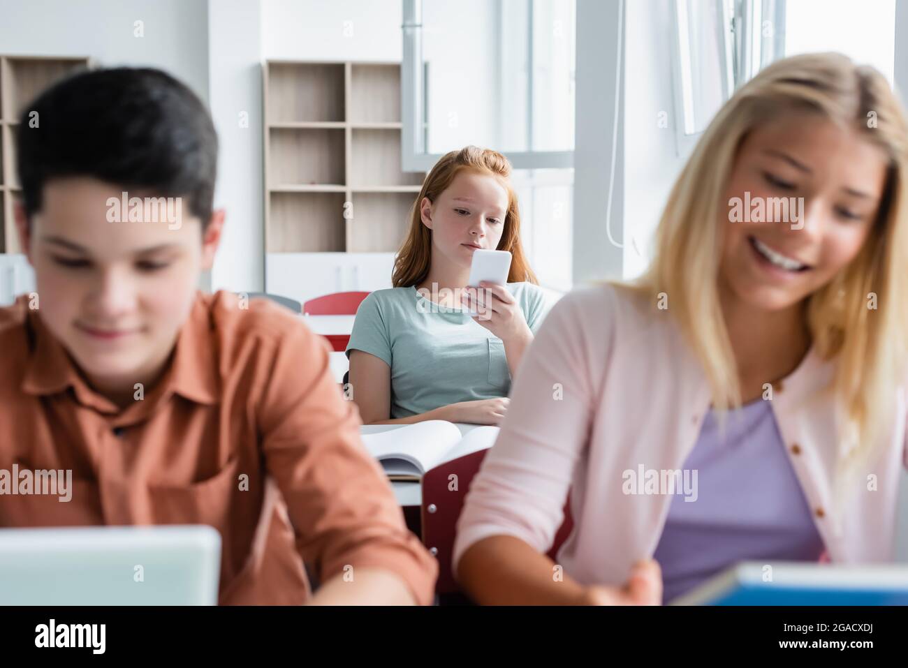 Schoolgirl using cellphone near blurred classmates in classroom Stock ...