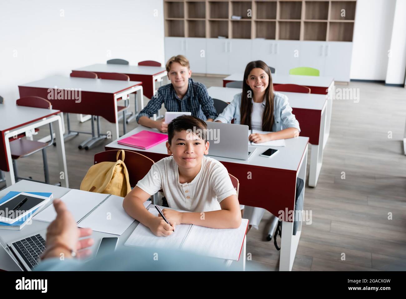 multicultural classmates looking at teacher on blurred foreground ...