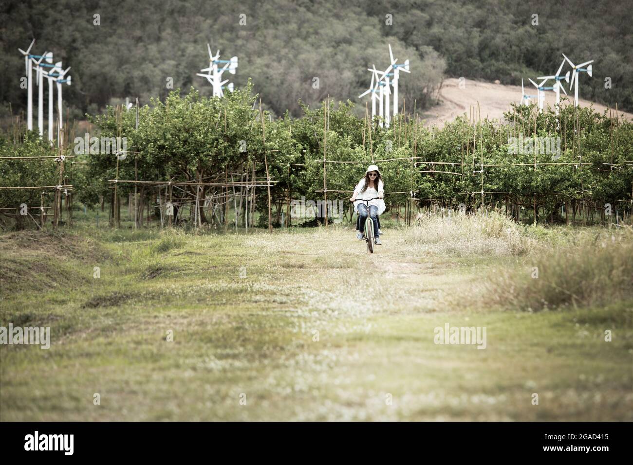 Woman riding bicycle in field with wind turbine in background vintage ...