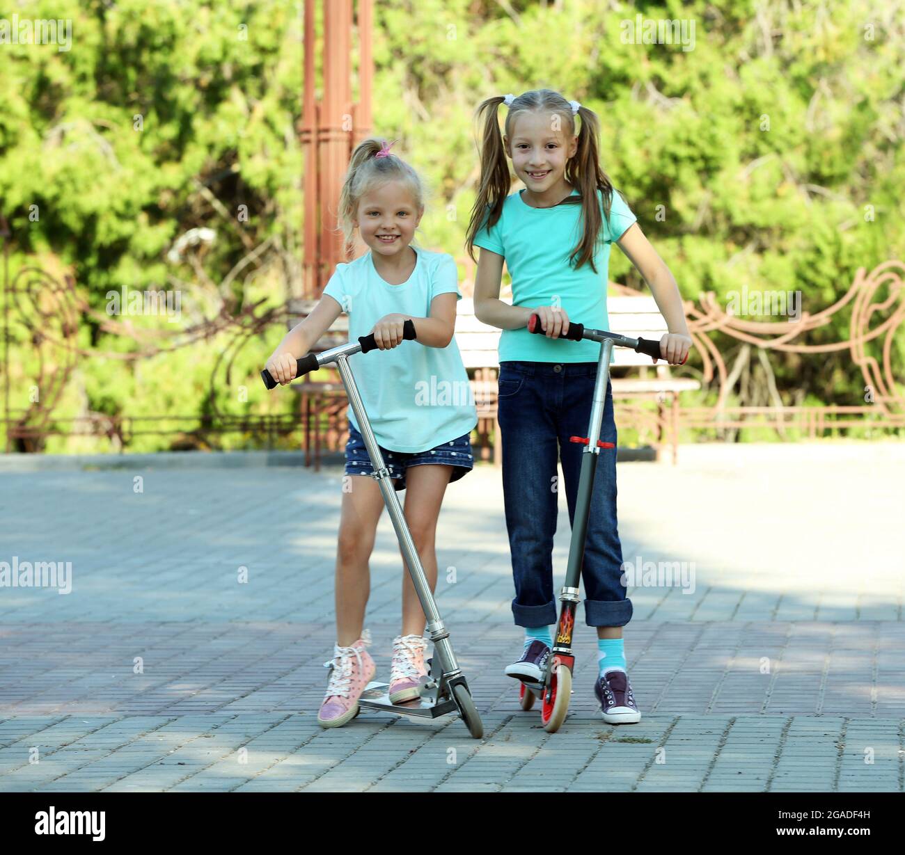 Small girls riding on scooters in park Stock Photo - Alamy