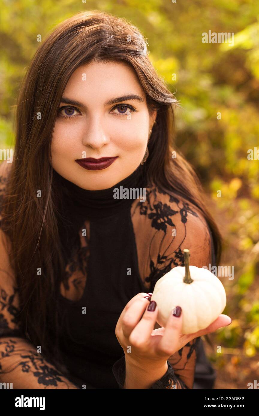 Young brunette female holding little white pumpkin in front of her face ...