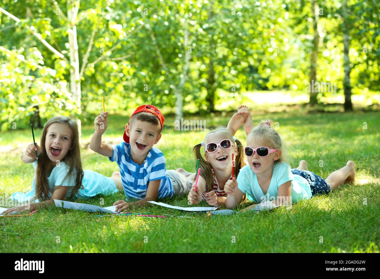 Happy active children lying on green grass and drawing in park Stock ...