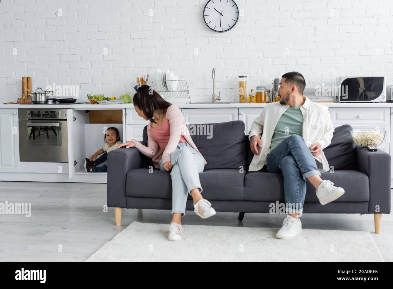 happy asian kid hiding in kitchen cabinet near parents on sofa Stock ...