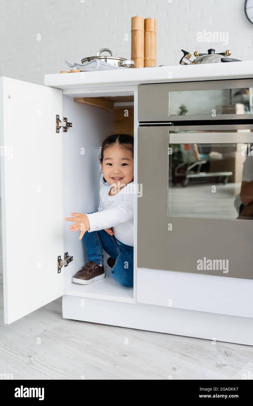 happy toddler asian kid hiding in kitchen cabinet Stock Photo - Alamy
