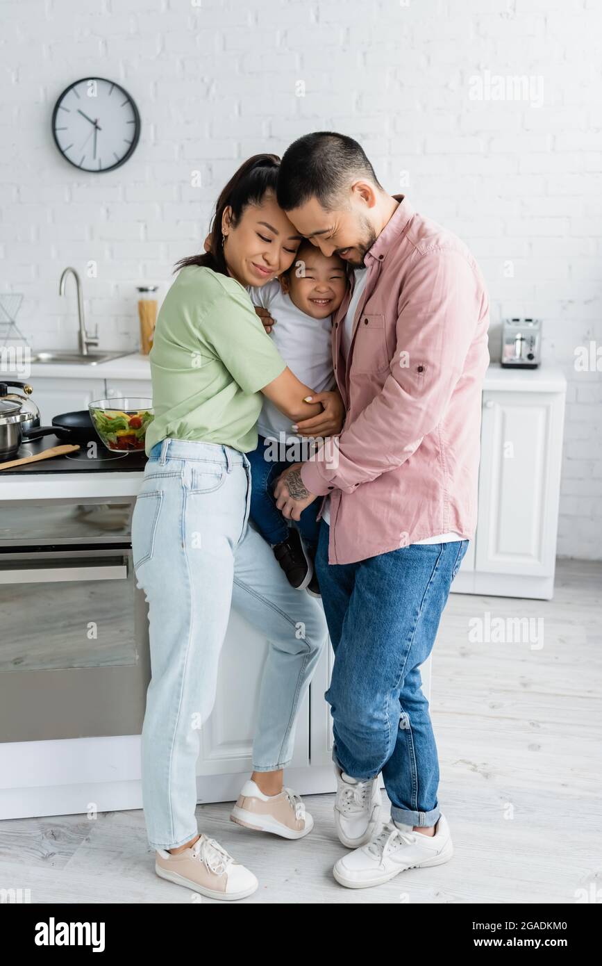 asian parents hugging with cheerful toddler daughter in kitchen Stock ...