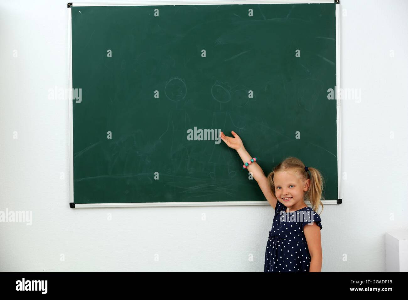 Little girl pointing at something at black chalkboard in classroom ...