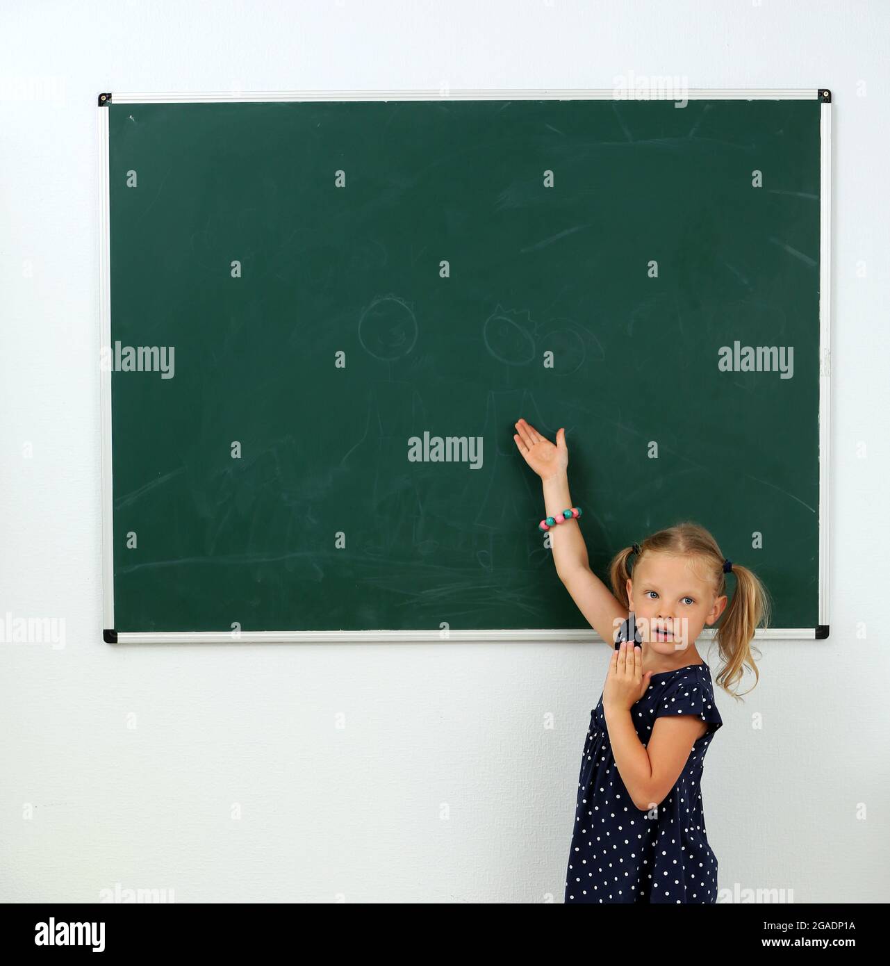 Little girl pointing at something at black chalkboard in classroom ...