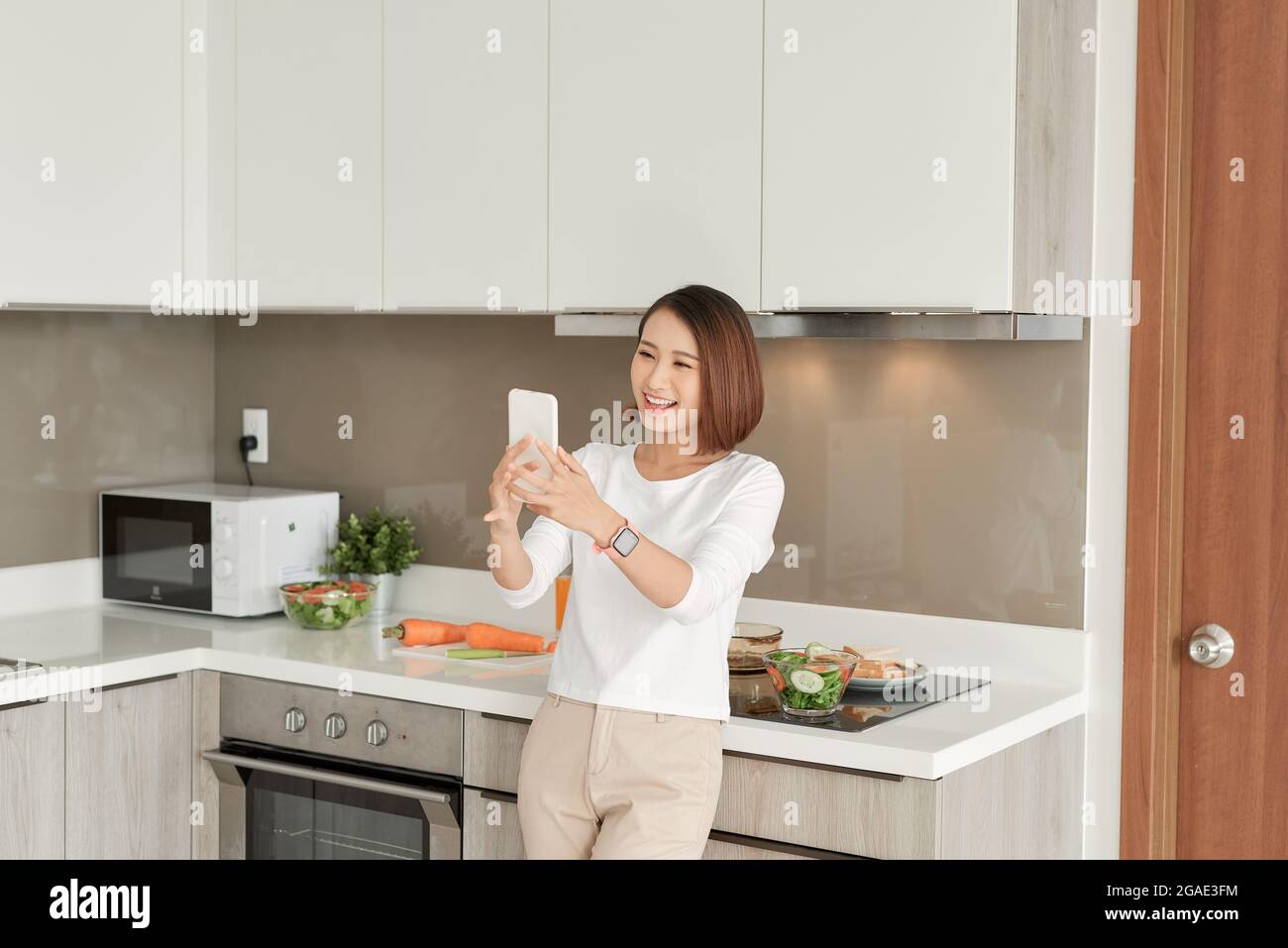 Young asian woman in the kitchen using mobile phone making video call ...