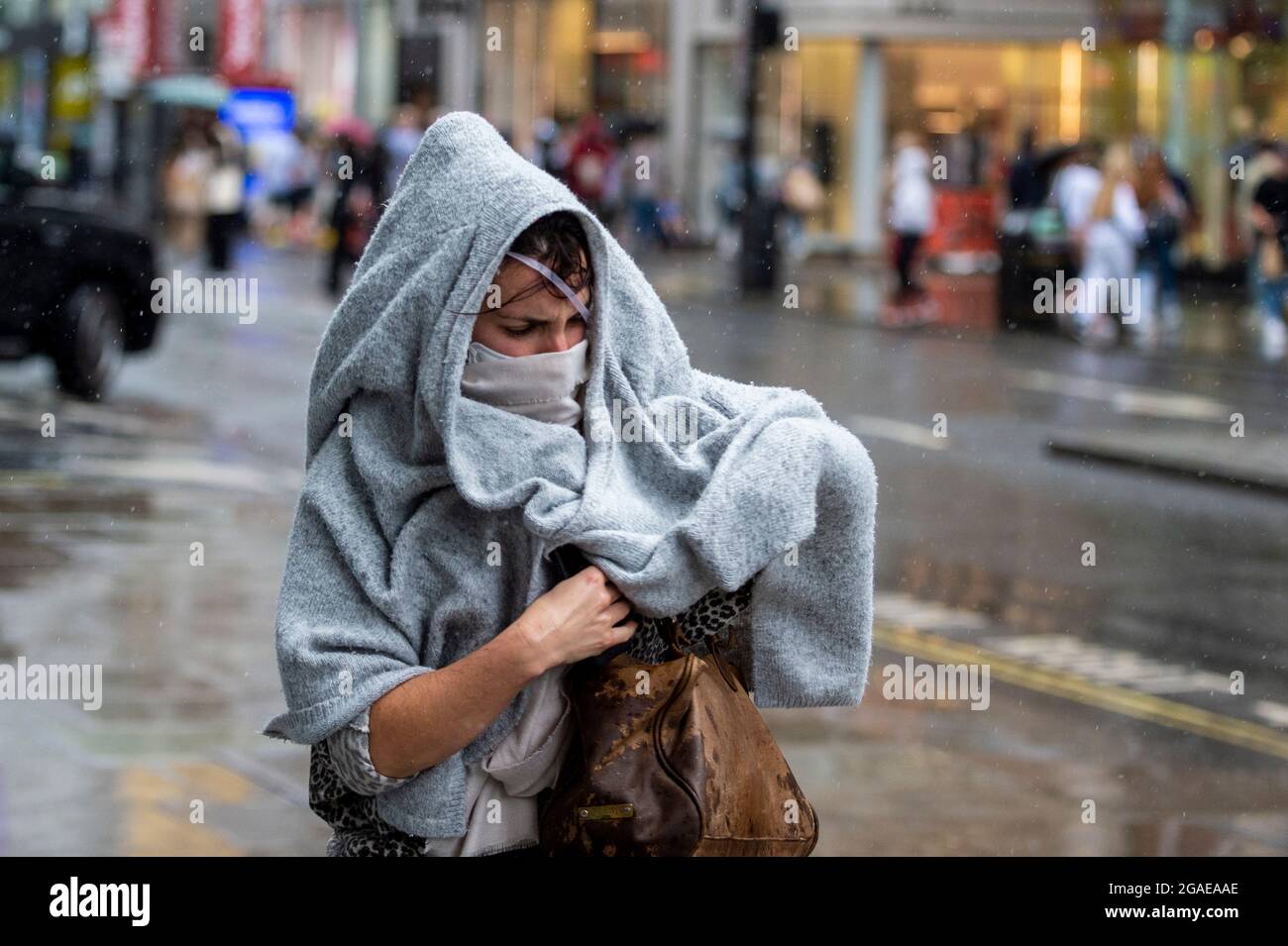London, UK. 30 July 2021. UK Weather - A woman tries to keep dry in ...
