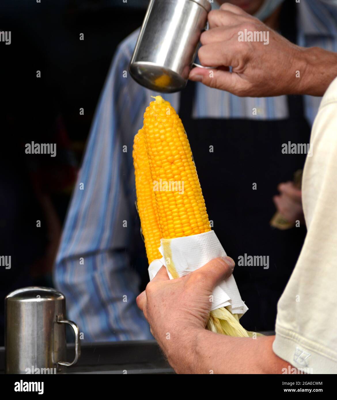 A man buys two ears of roasted corn-on-the-cob from a food stand at an ...