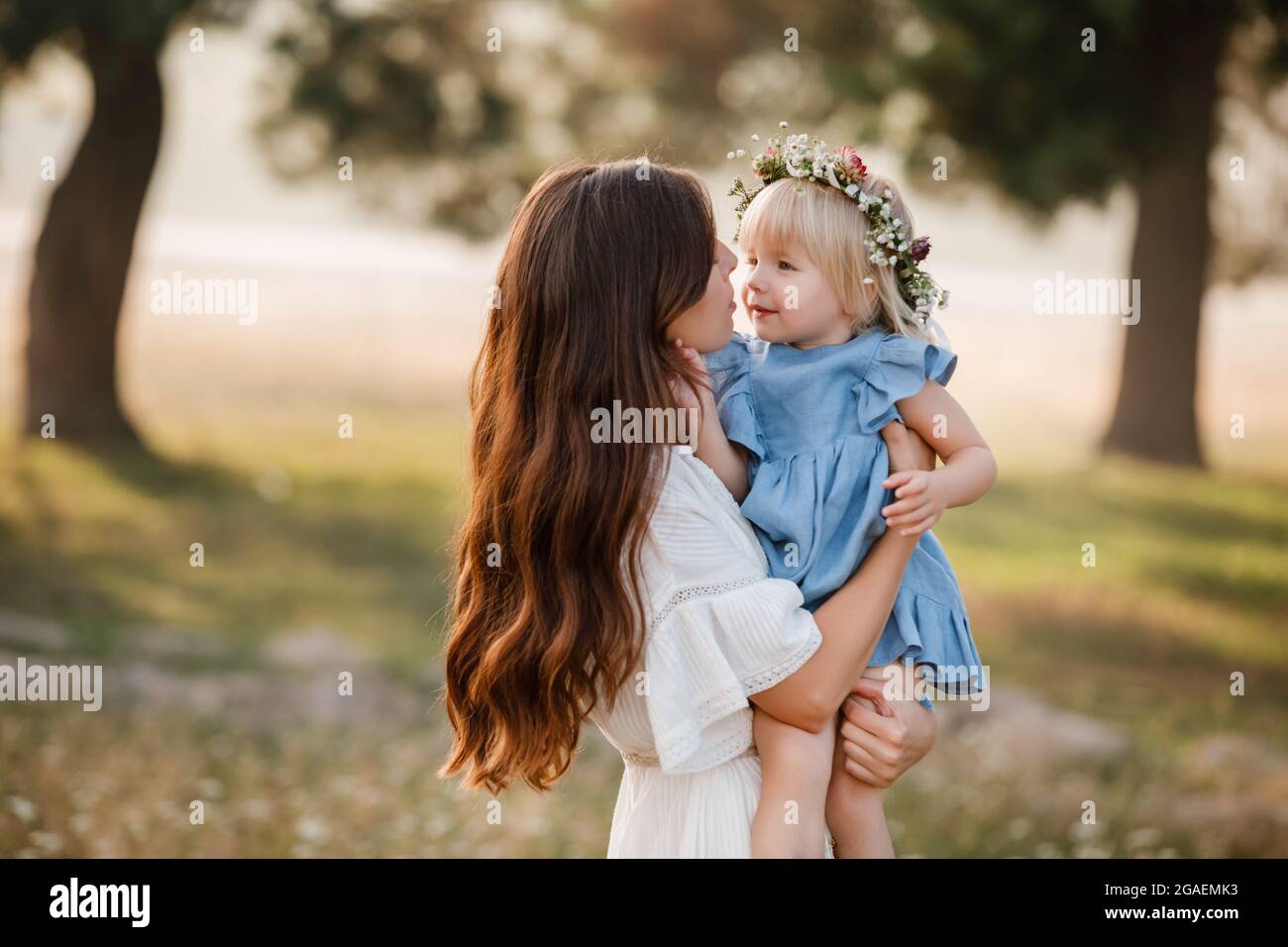 Young mother hugging her little daughter in the park on summer day. Family holiday in garden ...