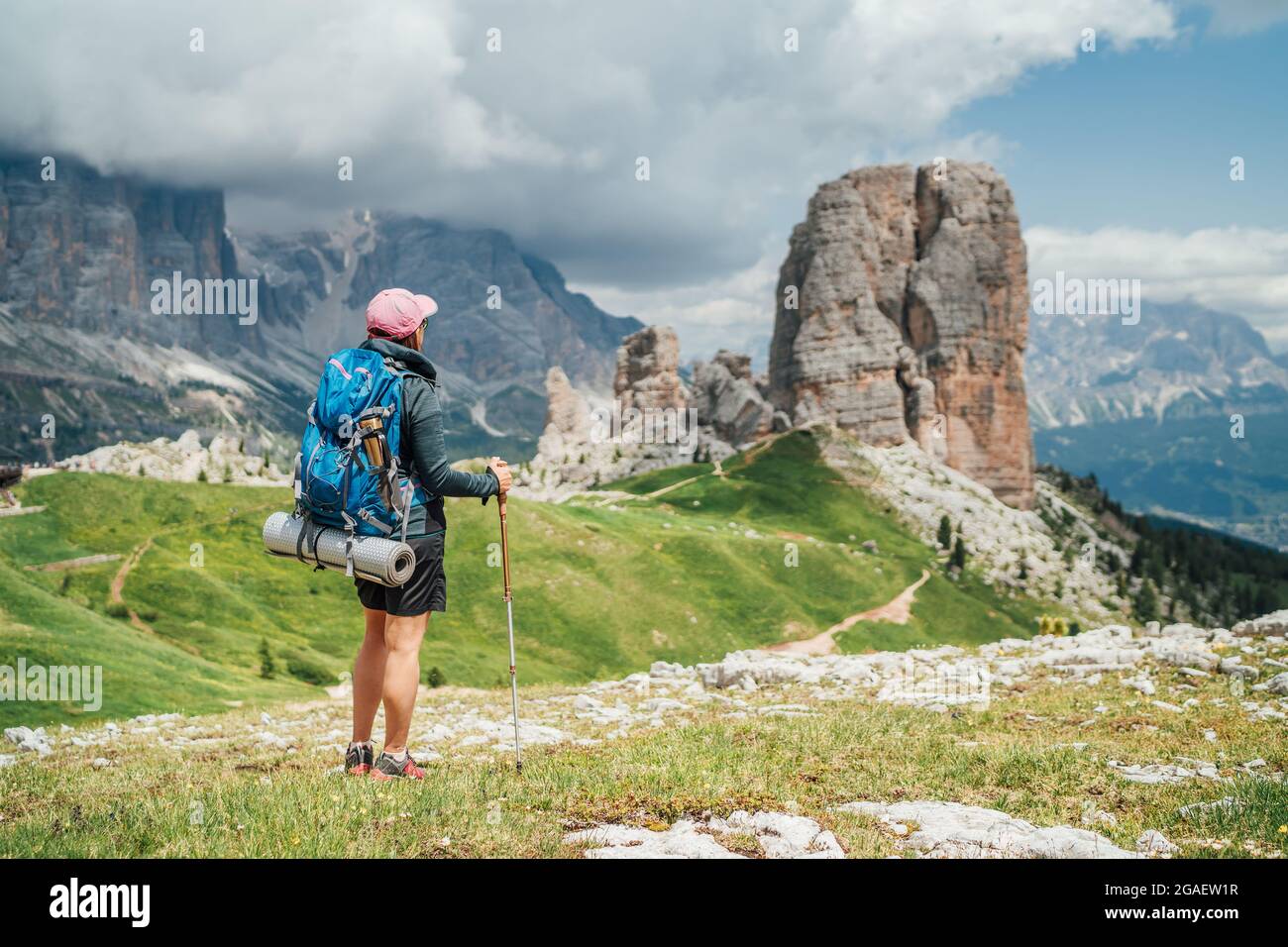Female trekker walking with backpack and trekking poles by green ...