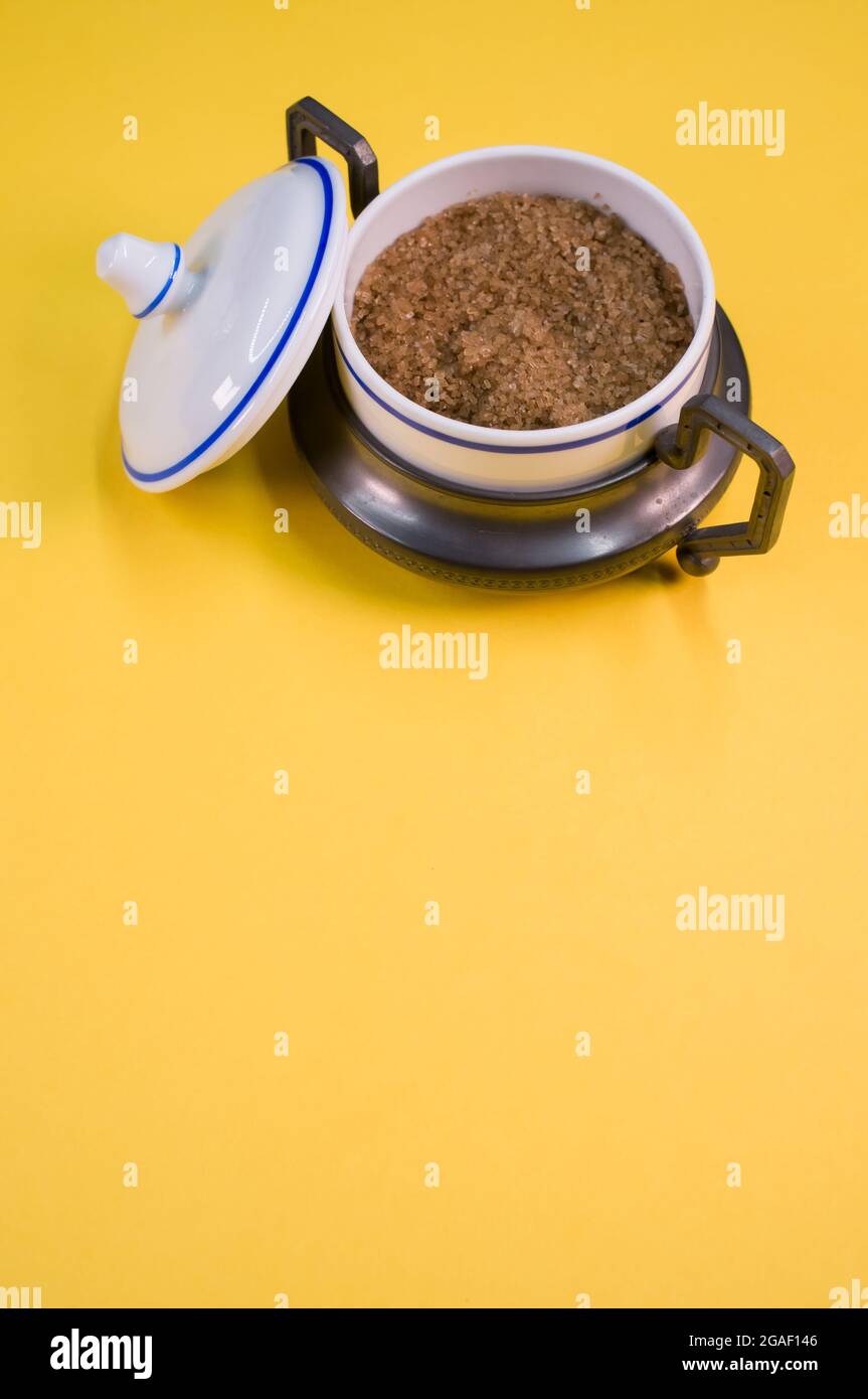 Vertical shot of brown sugar in a small ceramic jar on a yellow table ...