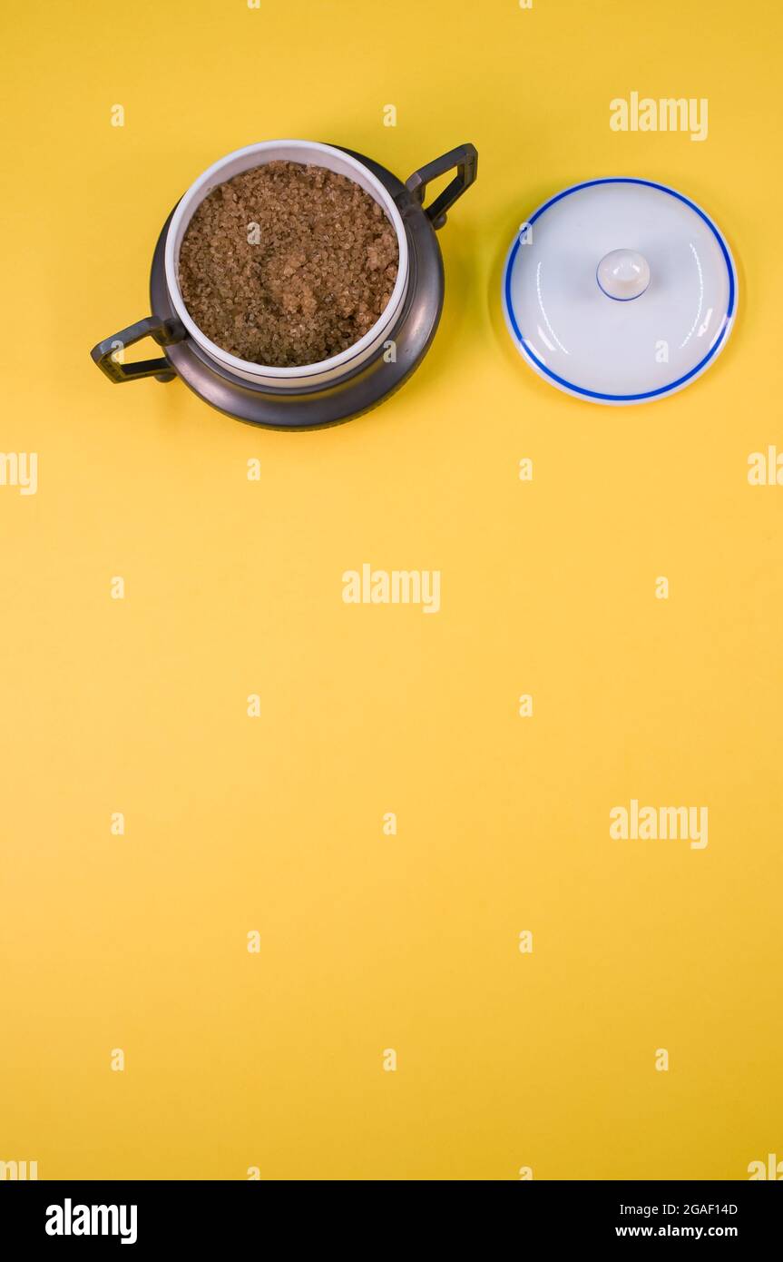 Vertical shot of brown sugar in a small ceramic jar on a yellow table ...
