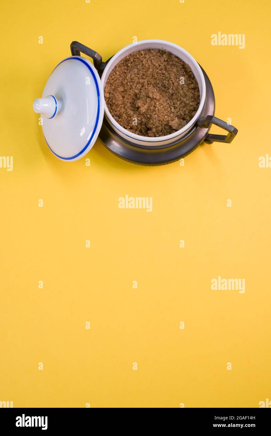 Vertical shot of brown sugar in a small ceramic jar on a yellow table ...