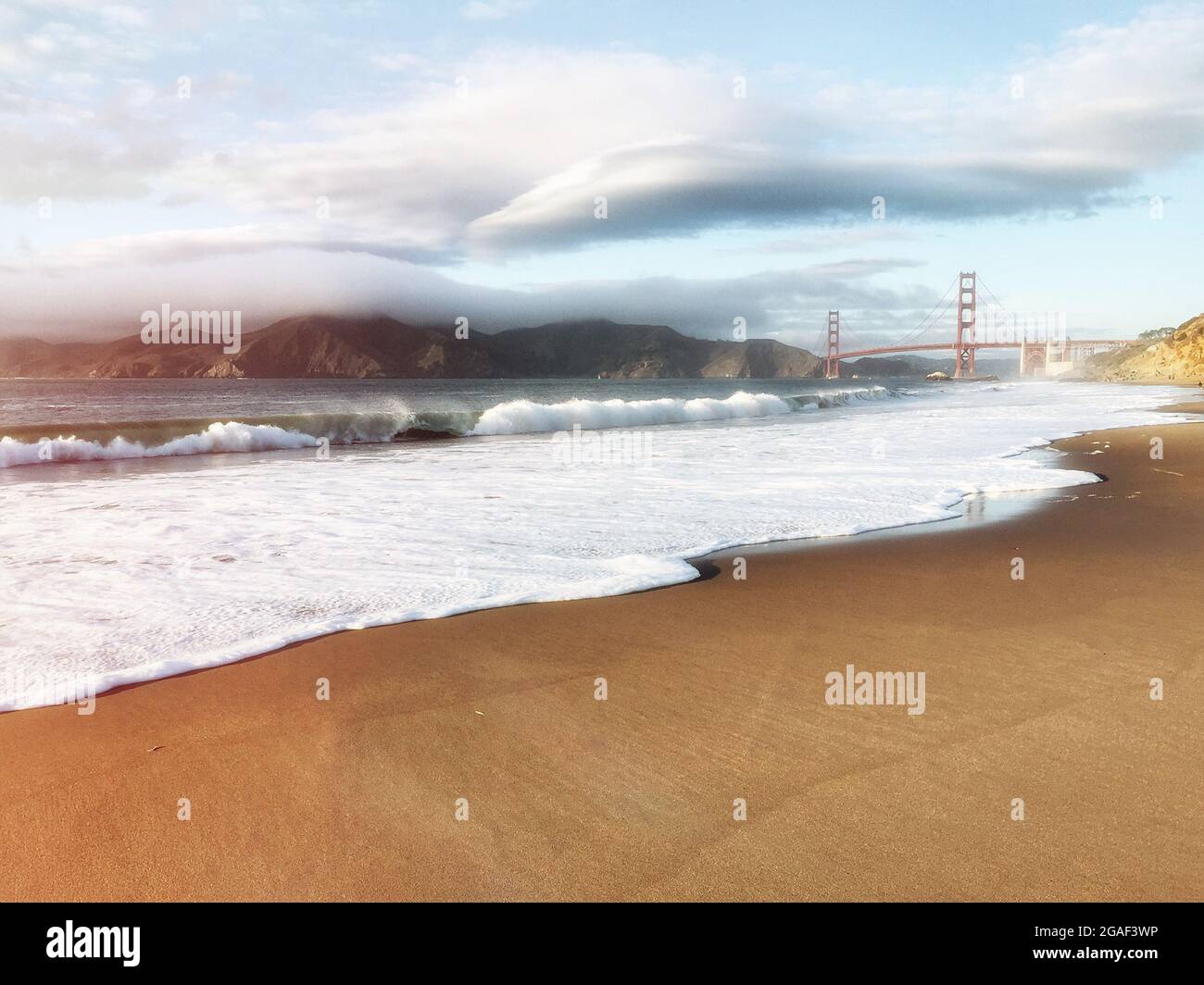 Golden gate bridge view from beach. Cloudy sky in background, waves in ...