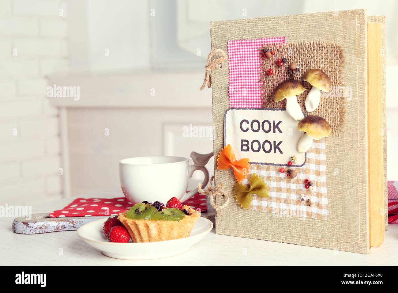 Decorated cookbook with cup of tea and tasty cake on white background ...