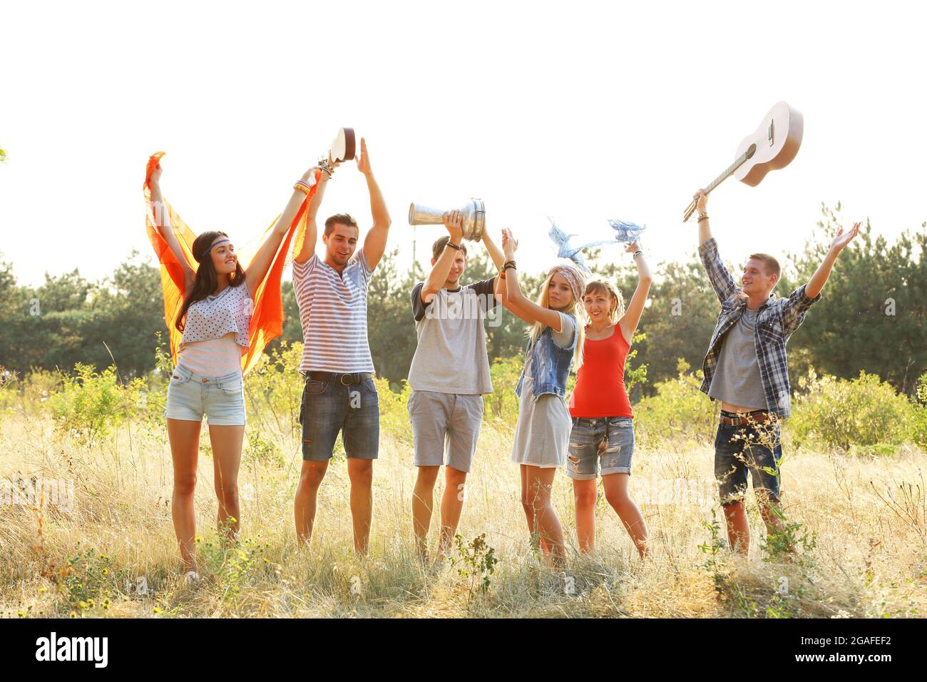 Joyful smiling friends dancing with raised hands in the forest outdoors ...