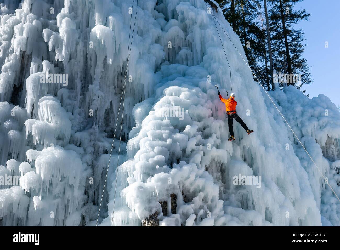 Male athlete climb cliff covered with ice, swinging the ice axe and ...