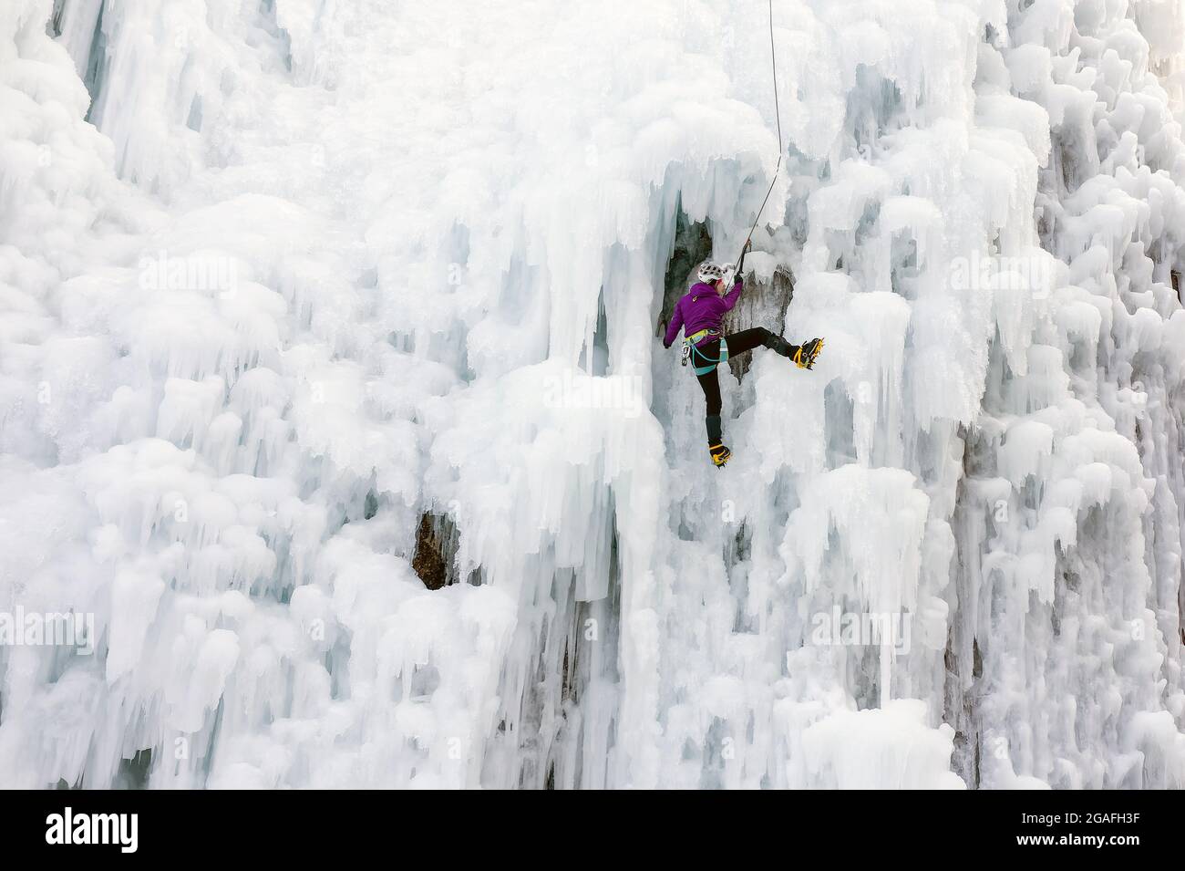 Alpinist woman with ice climbing equipment, axe and climbing ropes ...