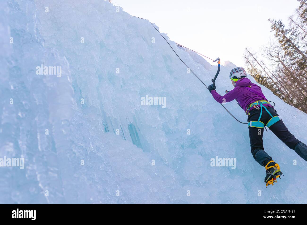 Female ice climber silhouette swinging ice axes on her way up vertical ...