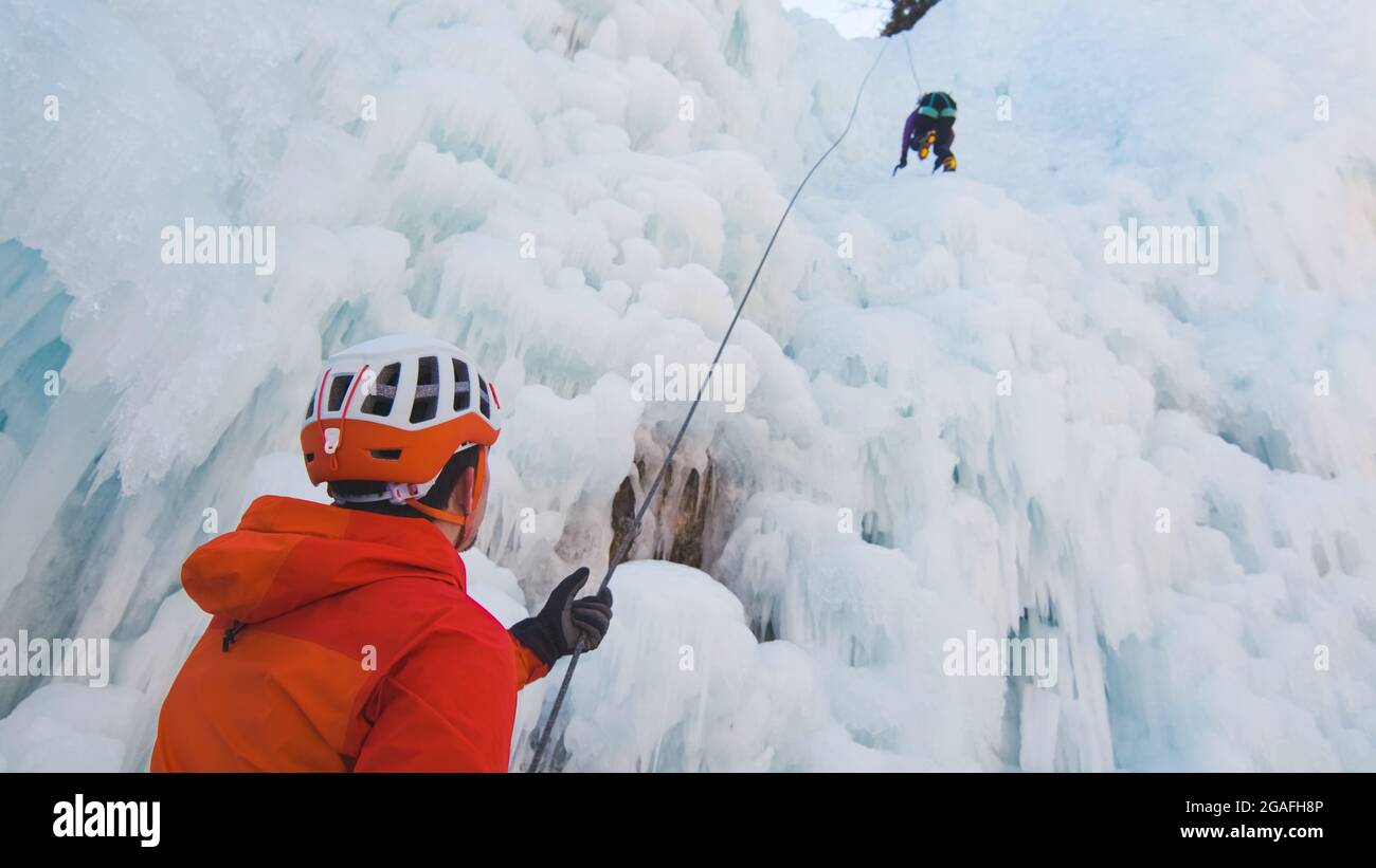 Man standing and controlling a safety top rope while female with ice ...