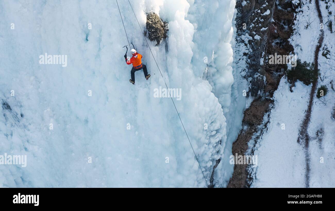 Aerial shot of a frozen waterfall, and a caucasian ice climber facing ...
