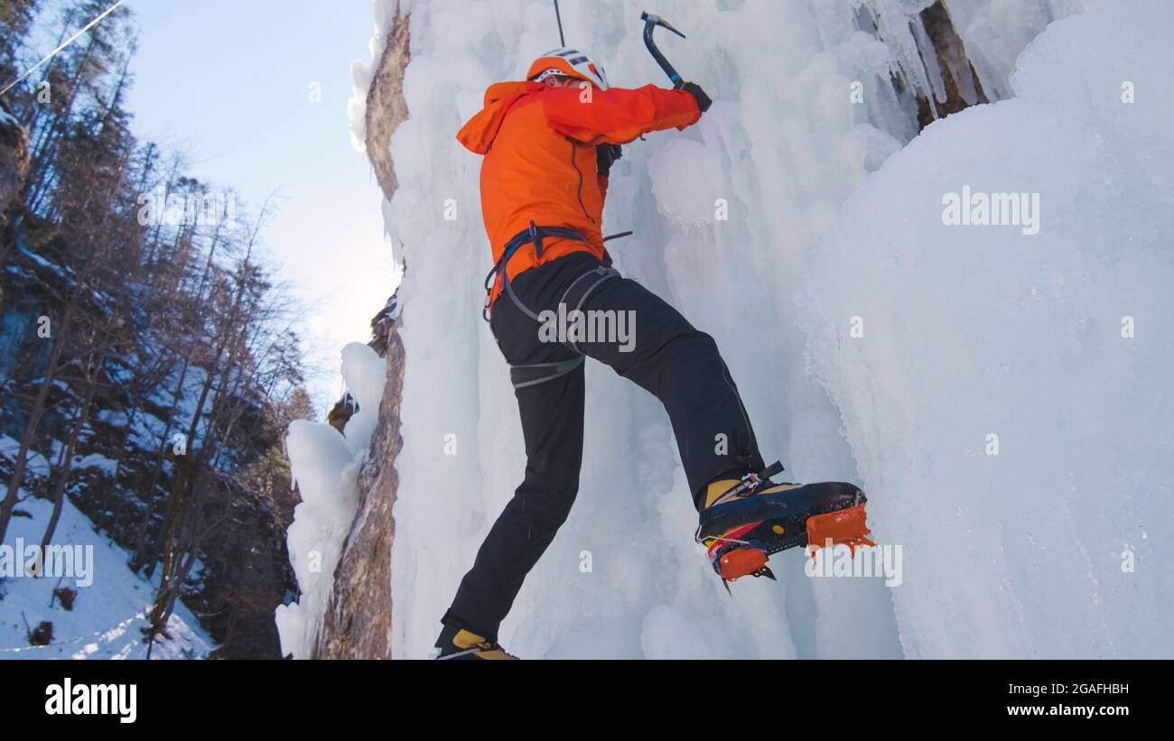Athlete climbing cliff covered with ice, using ice axes, and piercing ...