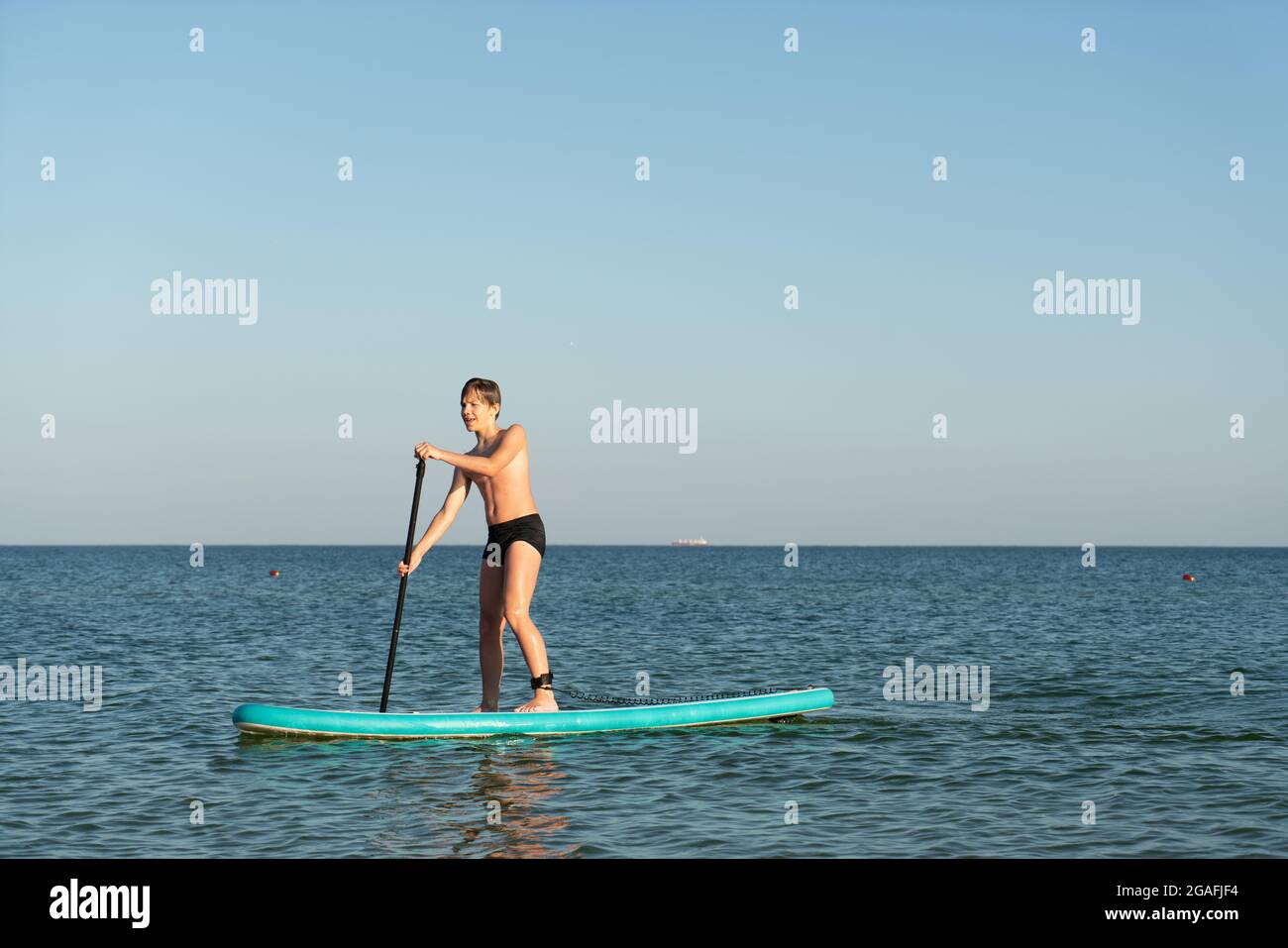 A 12 year old boy learns to stand on a SUP board in the sea near the ...