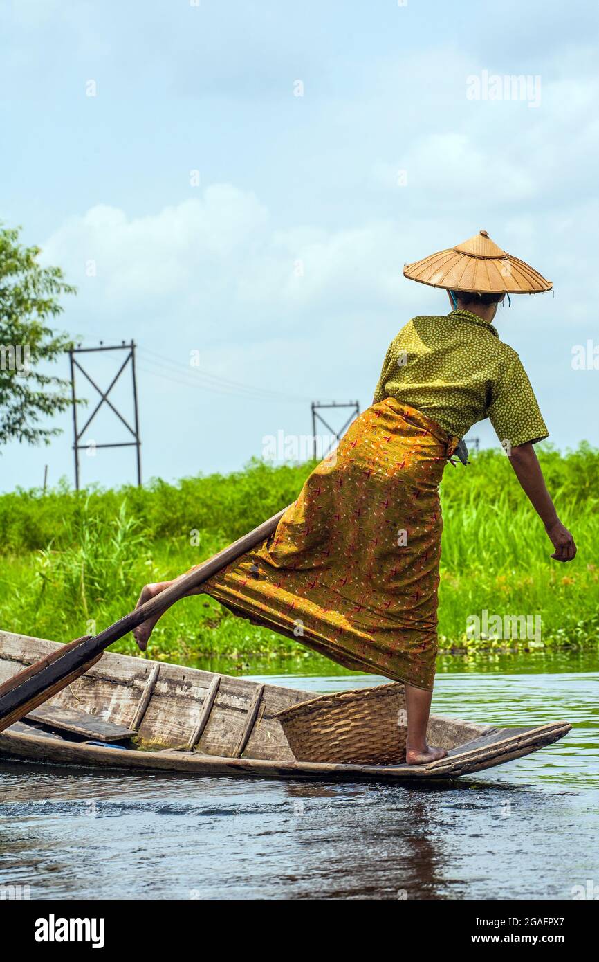 Burmese female wearing conical straw hat and colourful clothing leg ...