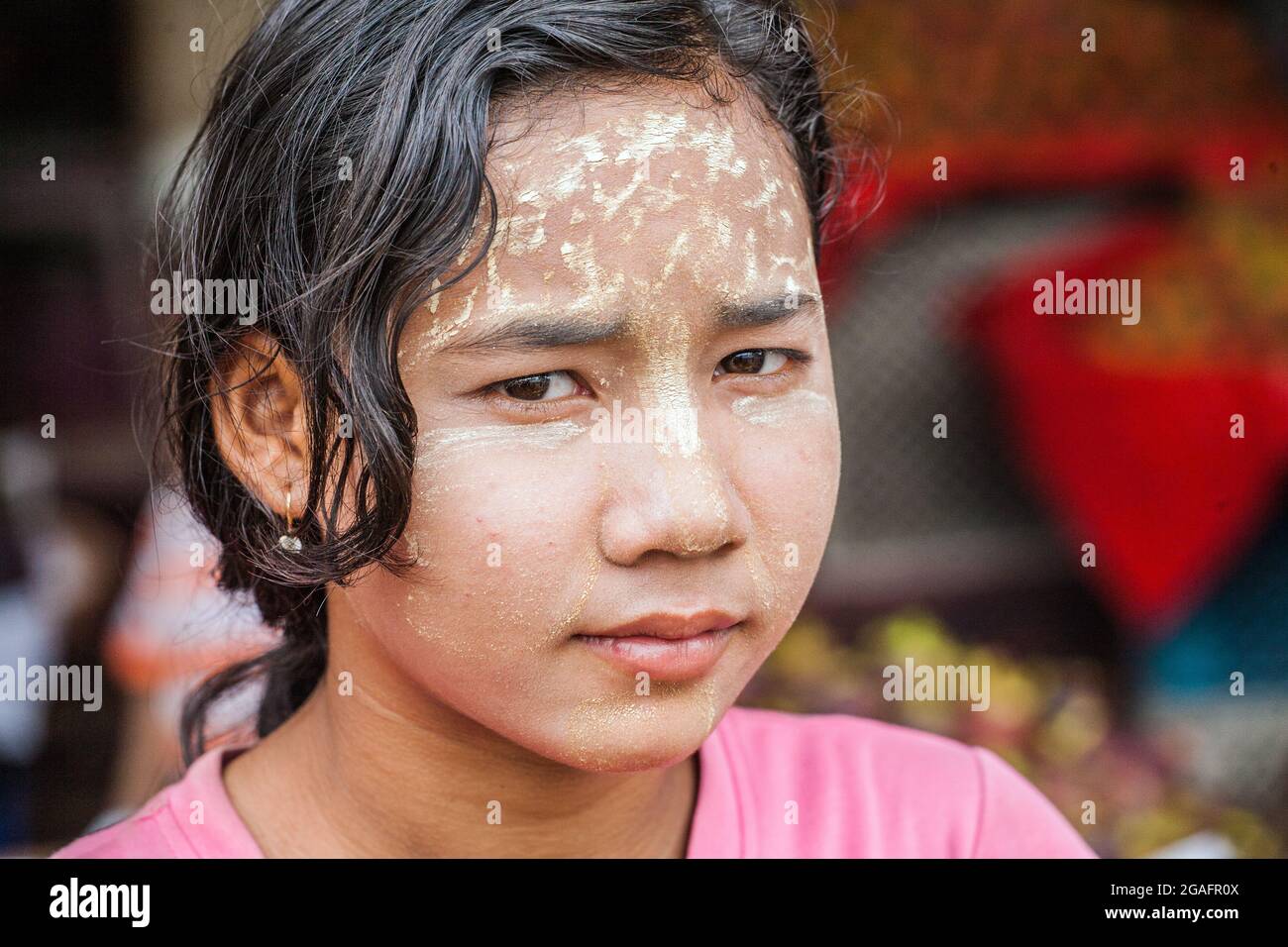 Pretty young Burmese girl with thanaka face powder on forehead and nose posing for photograph ...