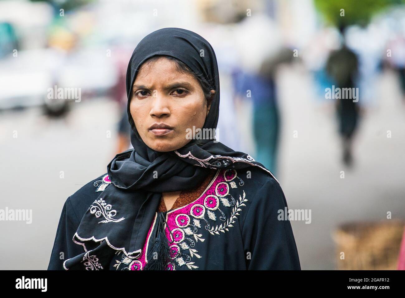 Burmese Muslim female wearing hijab stands staring frowning at camera ...