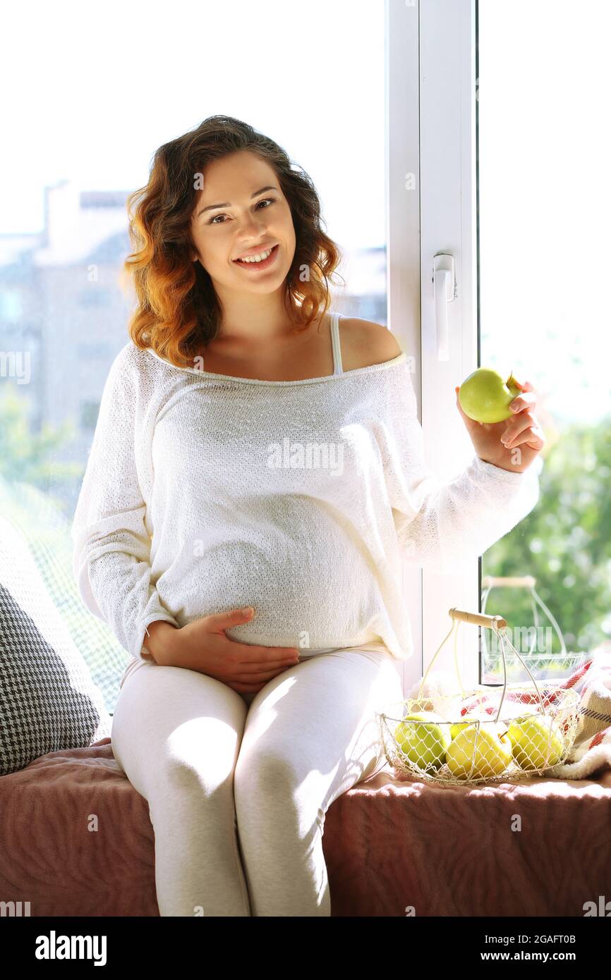 Pregnant woman sitting on window board in the room with basket of ...