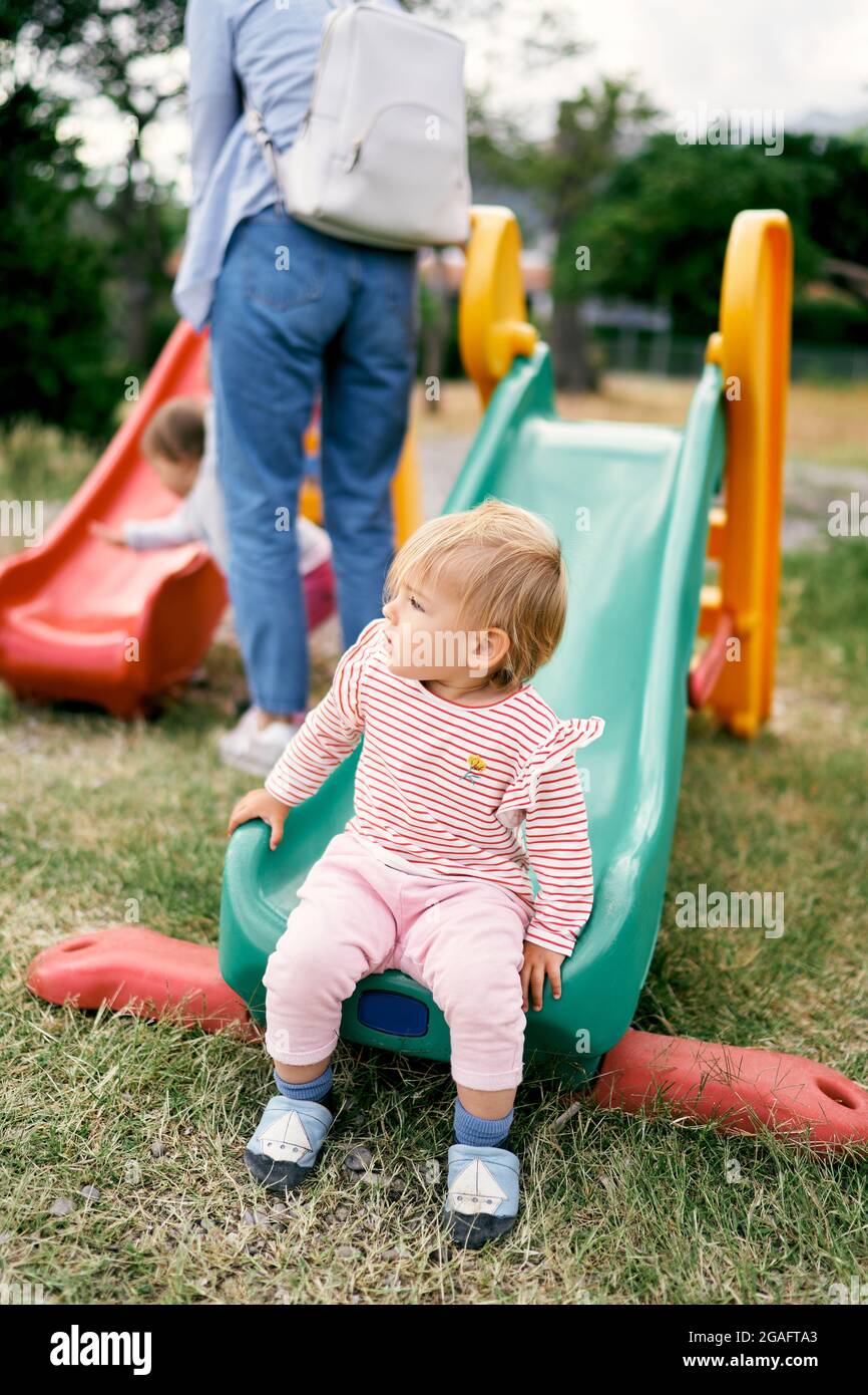 Kid sits on a children's slide on a playground in a green park Stock ...