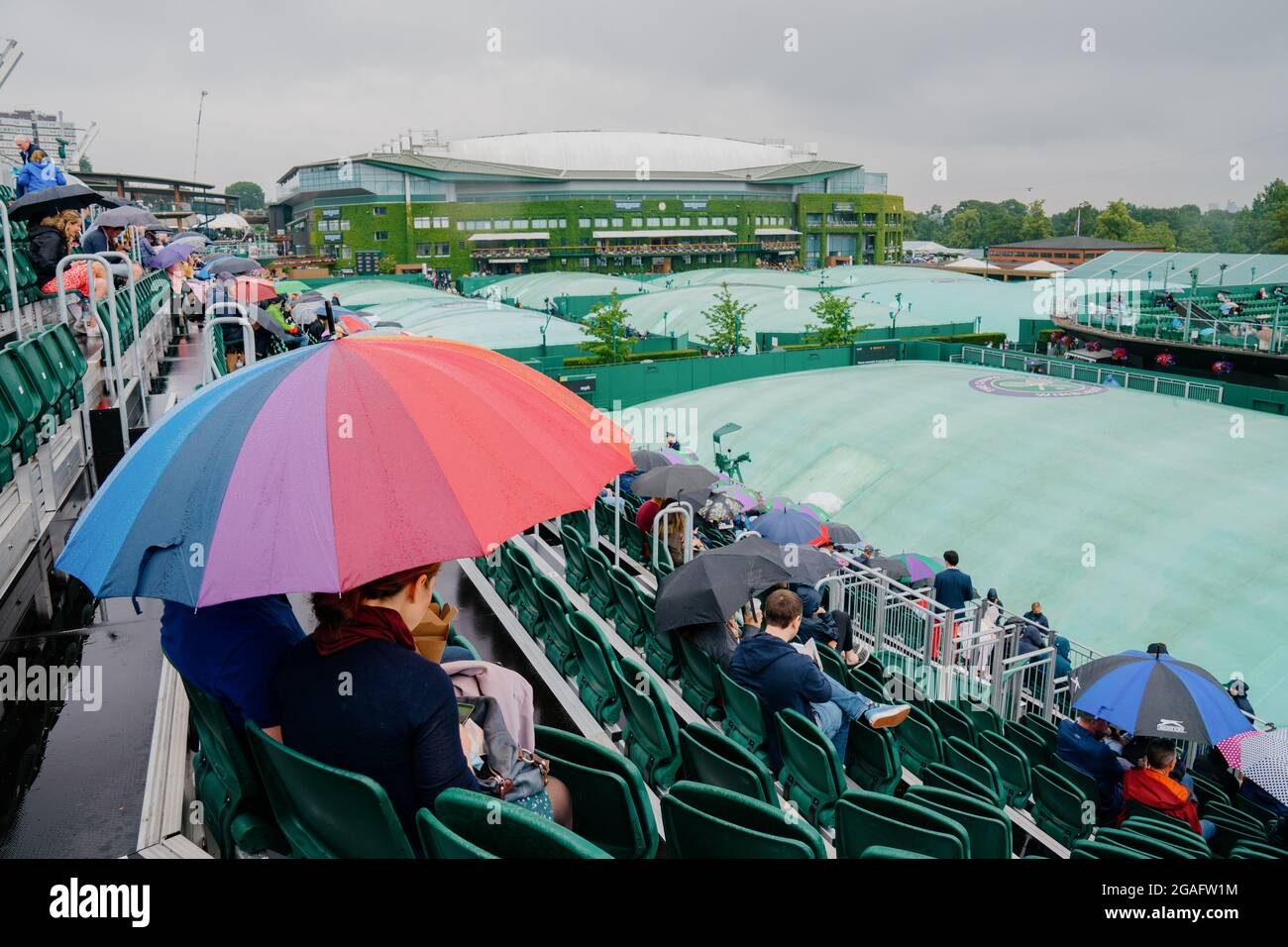Spectators huddle under umbrellas on Court 12 during The Wimbledon ...
