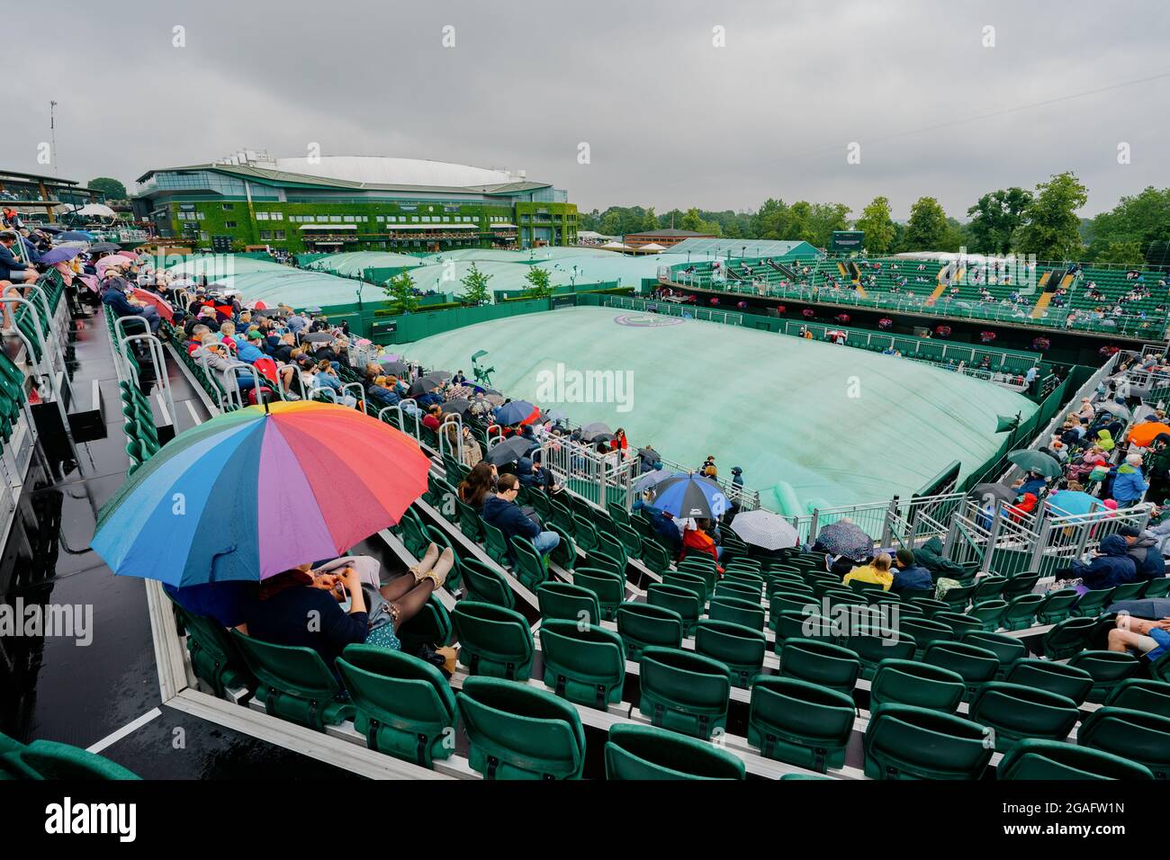 Spectators huddle under umbrellas on Court 12 during The Wimbledon ...