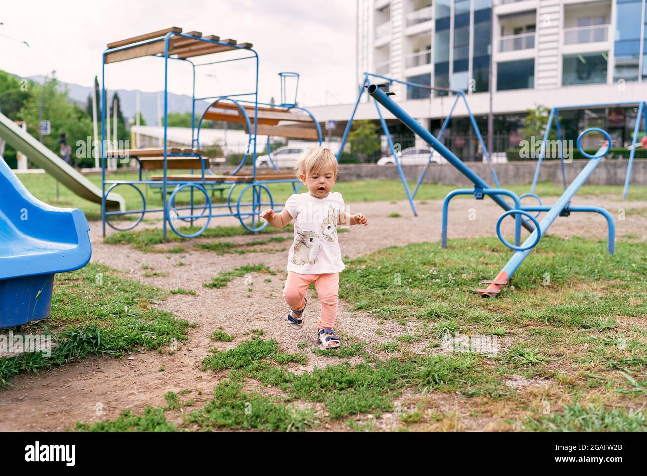 Little girl runs along the playground against the background of an ...