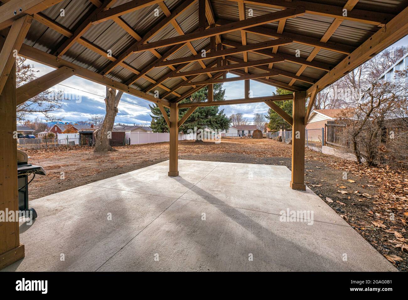 Covered patio in a large backyard with trees and fallen dry leaves ...