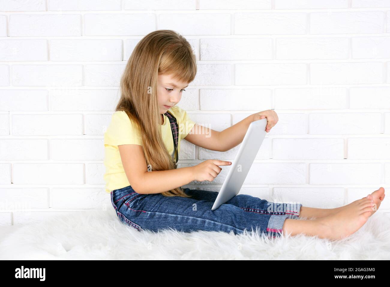 Little girl with tablet on brick wall background Stock Photo - Alamy