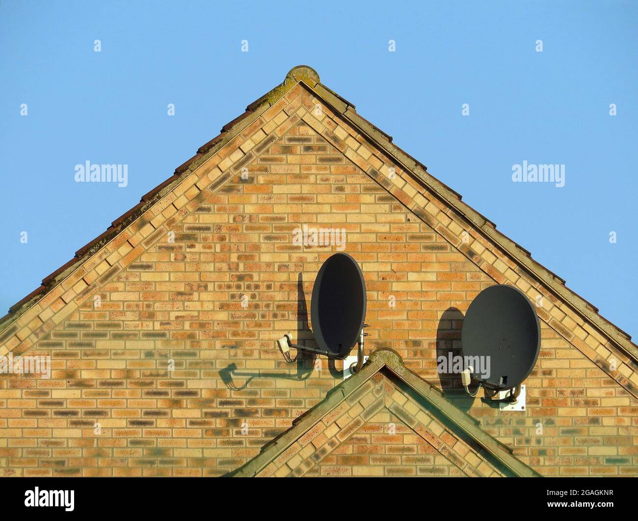 Close up of Two black TV satellite dishes on the side of a house with a ...