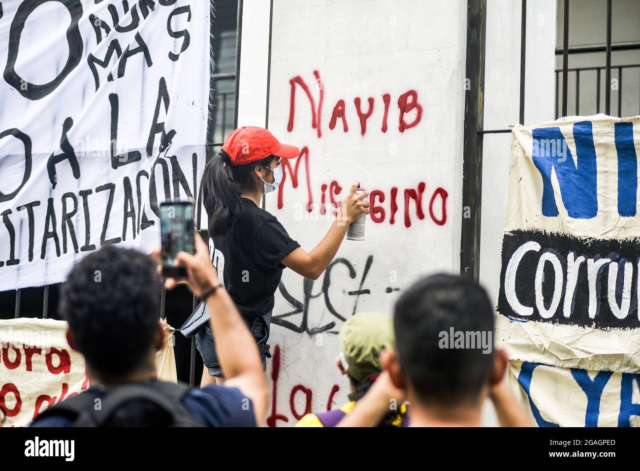 A demonstrator spray paints a wall with anti-Nayib Bukele messages ...