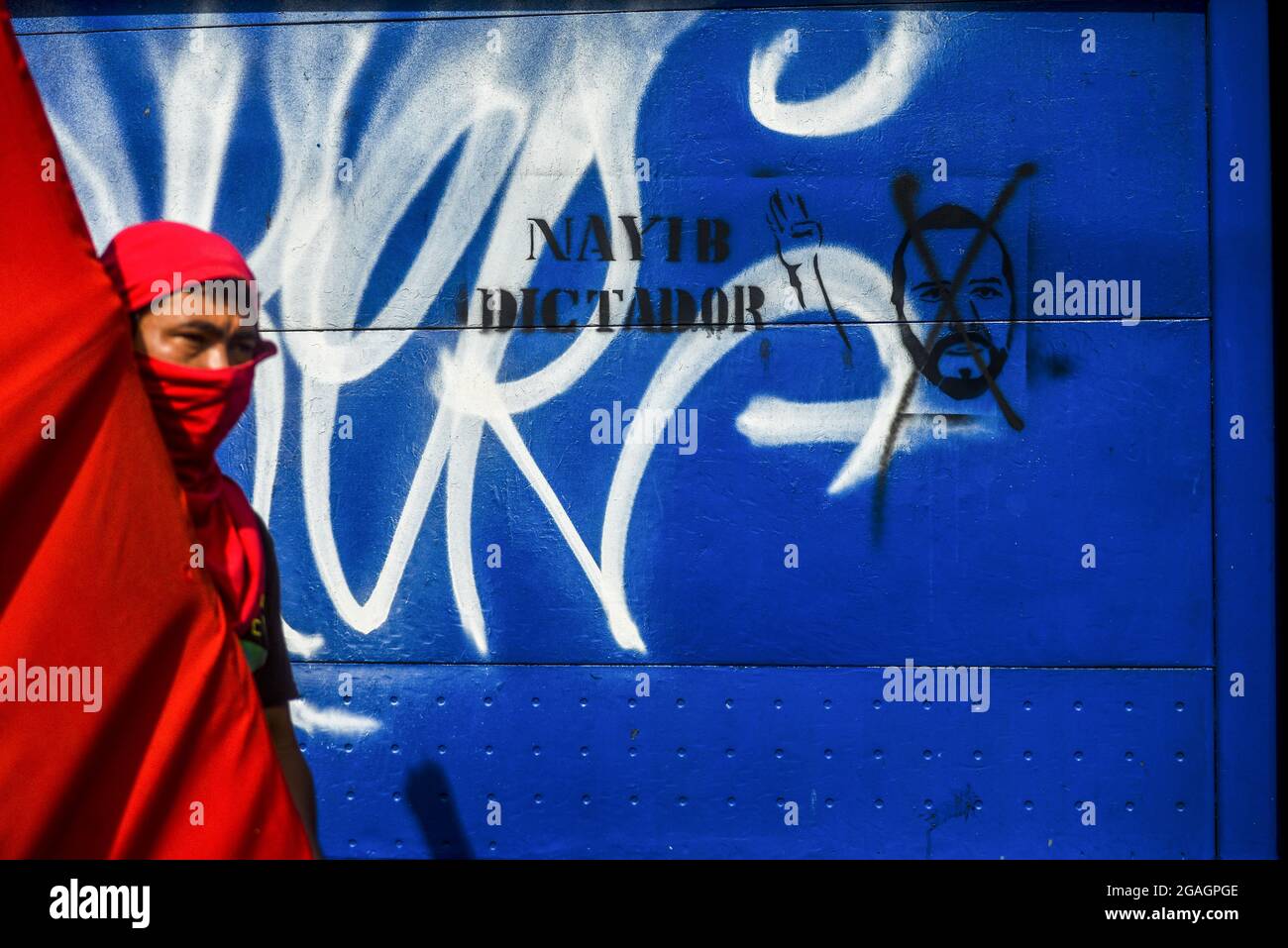 A demonstrator holding a banner marches past a graffiti reading "Bukele ...